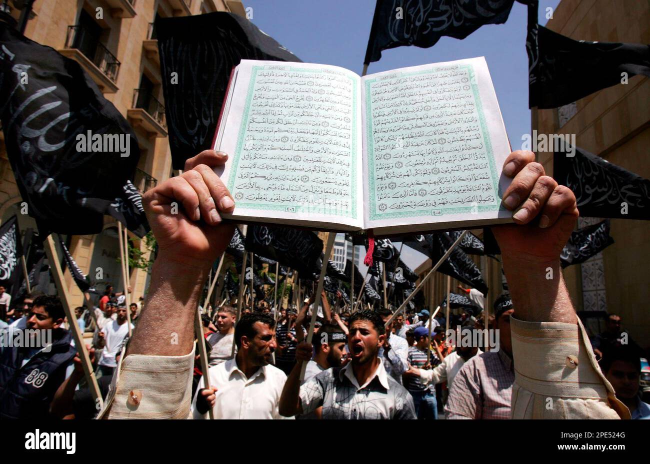 A Sunni Muslim fundamentalist holds the Quran as others wave flags ...