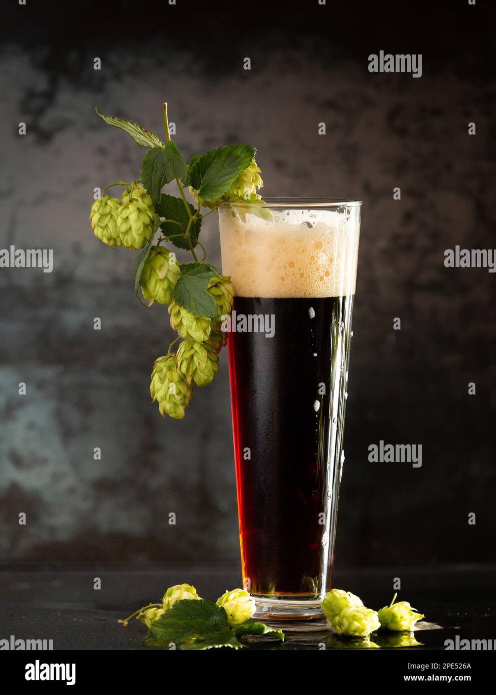 dark beer in a mug and green hop on wooden table on brown background ...