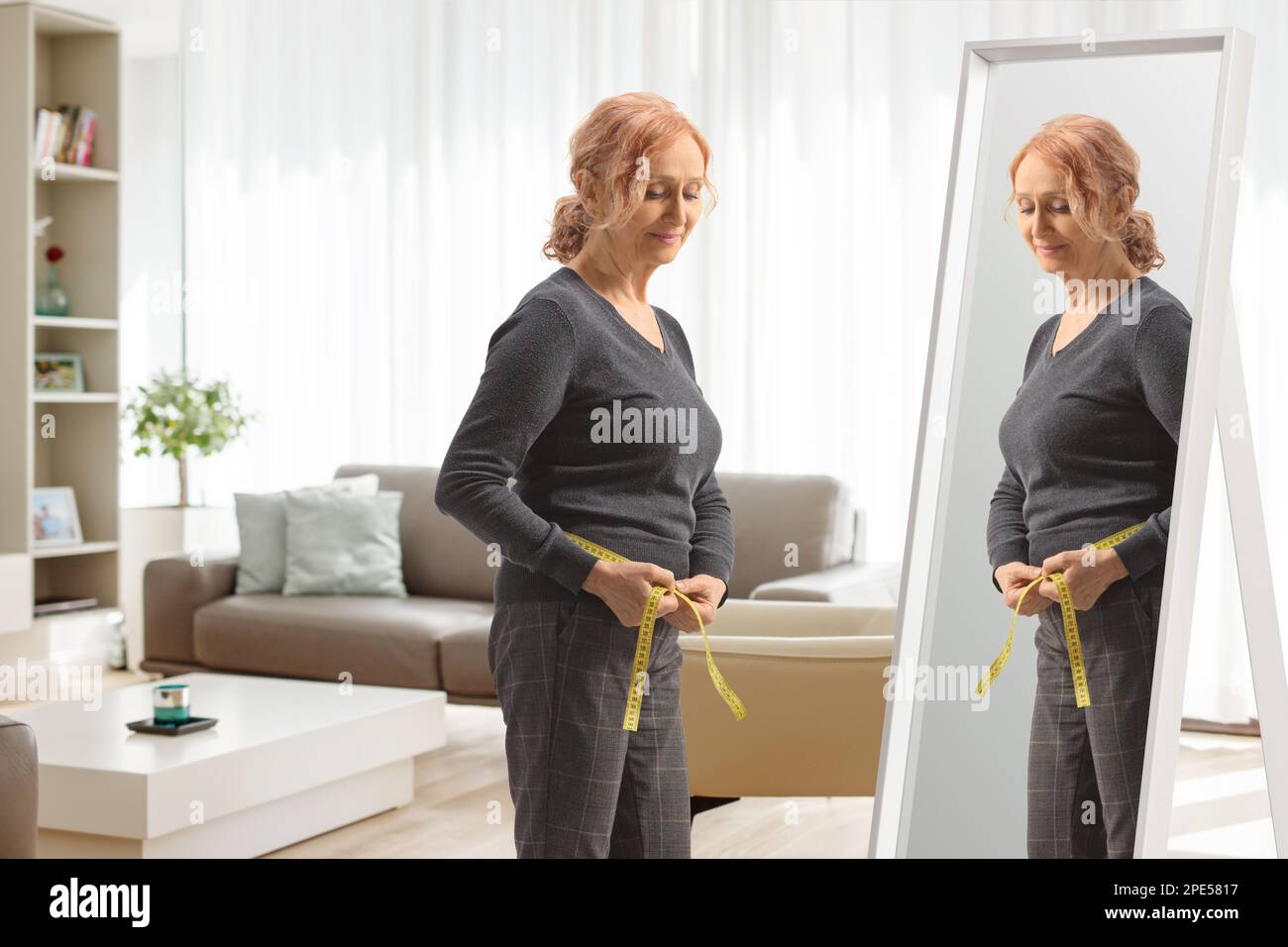 Mature woman measuring waist with a tape in front of a mirror at home ...