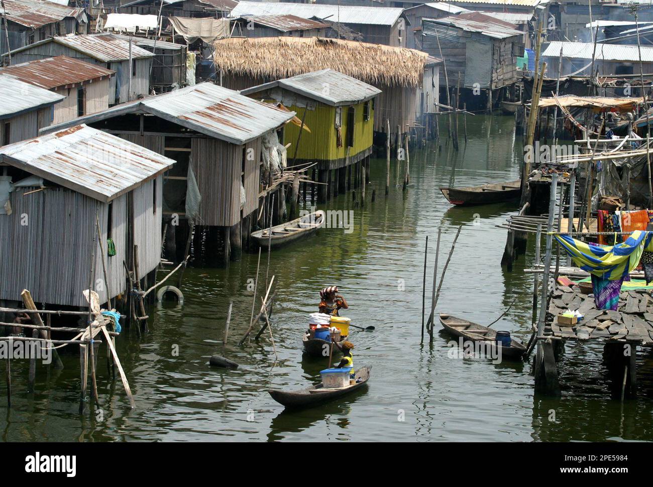 Women ride on a canoe pass wooden and tin houses built on water in ...