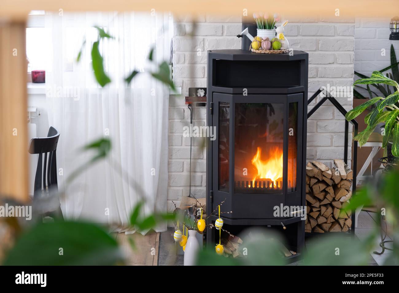 Easter decor near fireplace stove with fire and firewood. Cozy home ...