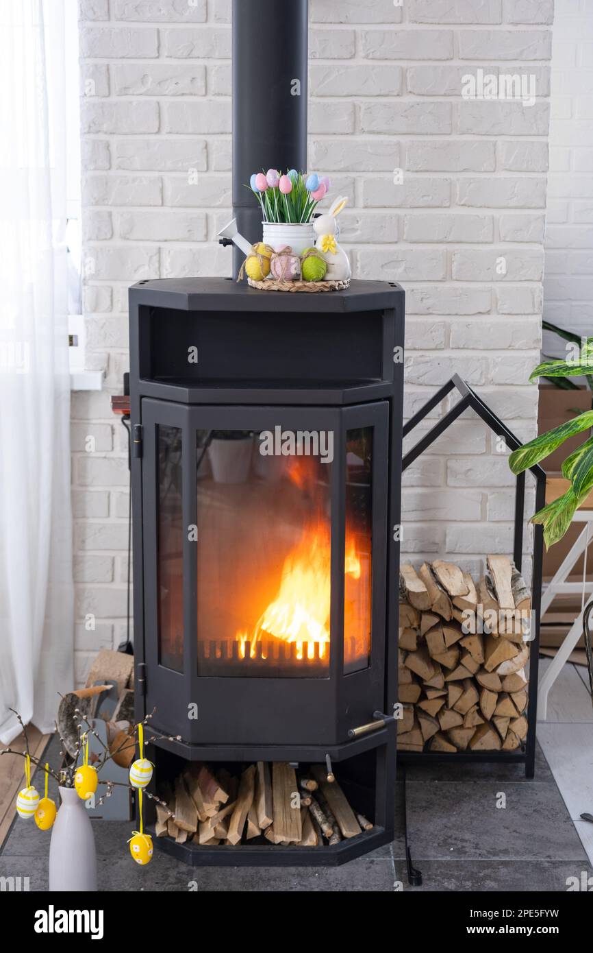 Easter decor near fireplace stove with fire and firewood. Cozy home ...