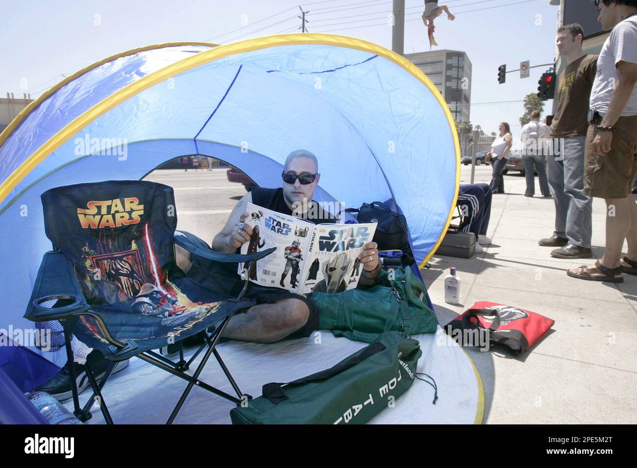 Brandon Flores takes shelter from the sun as he waits in line on a ...