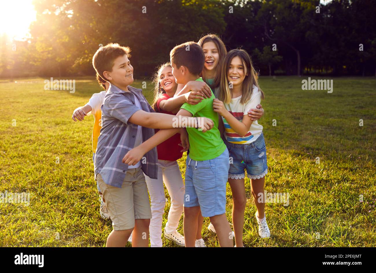 Cheerful children girls and boys hugging each other on sunny lawn at ...