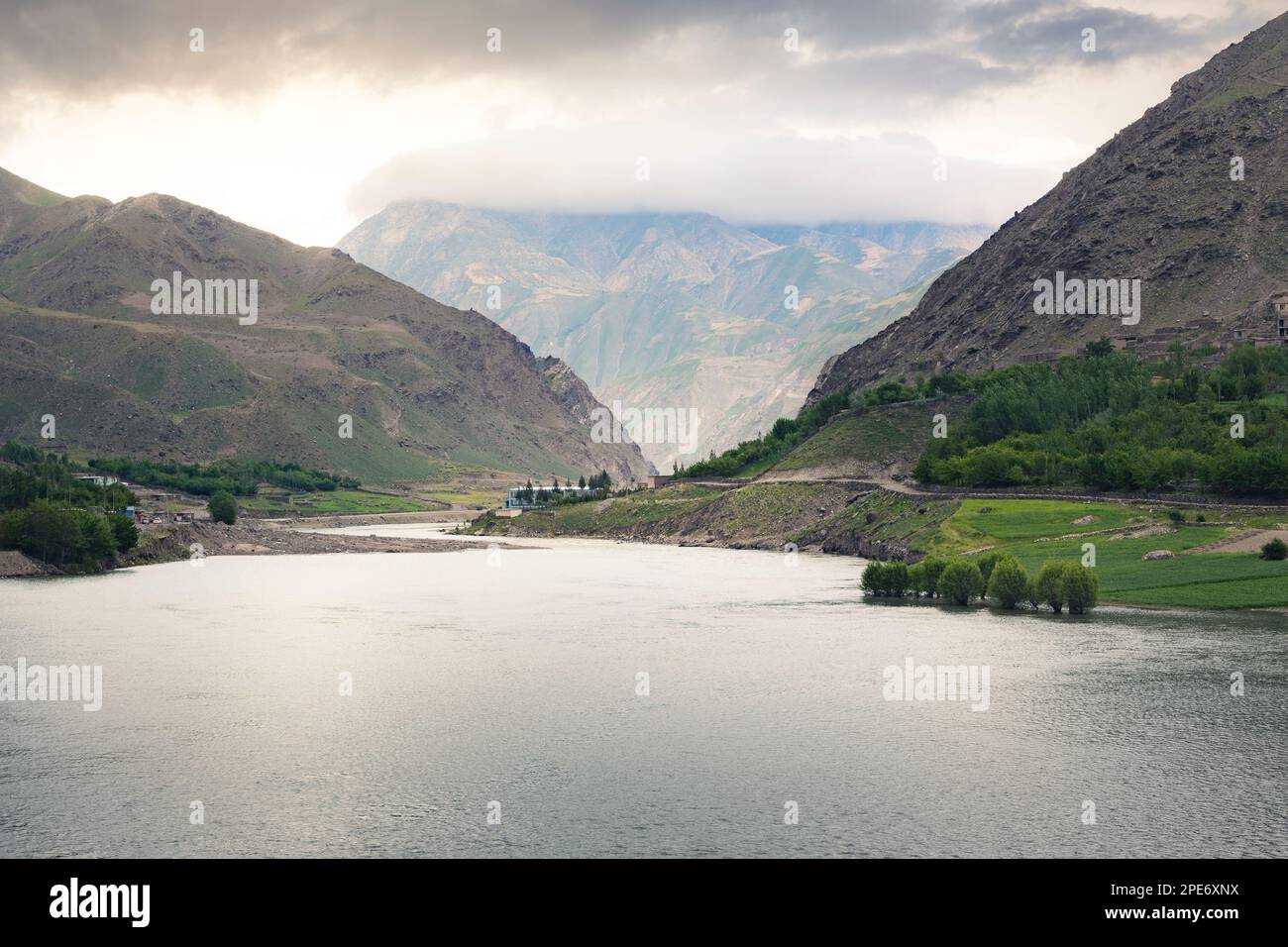 A moody photo of Kokcha River and trees with the mountains in the ...