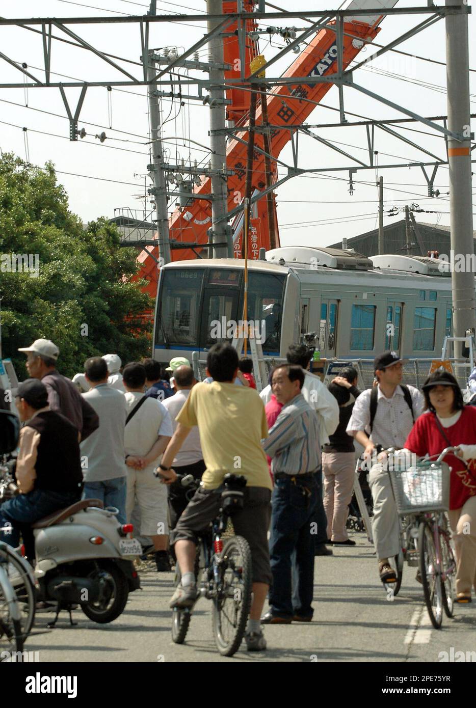 Residents look on as the rear car of a derailed train remains on the tracks in Amagasaki ...