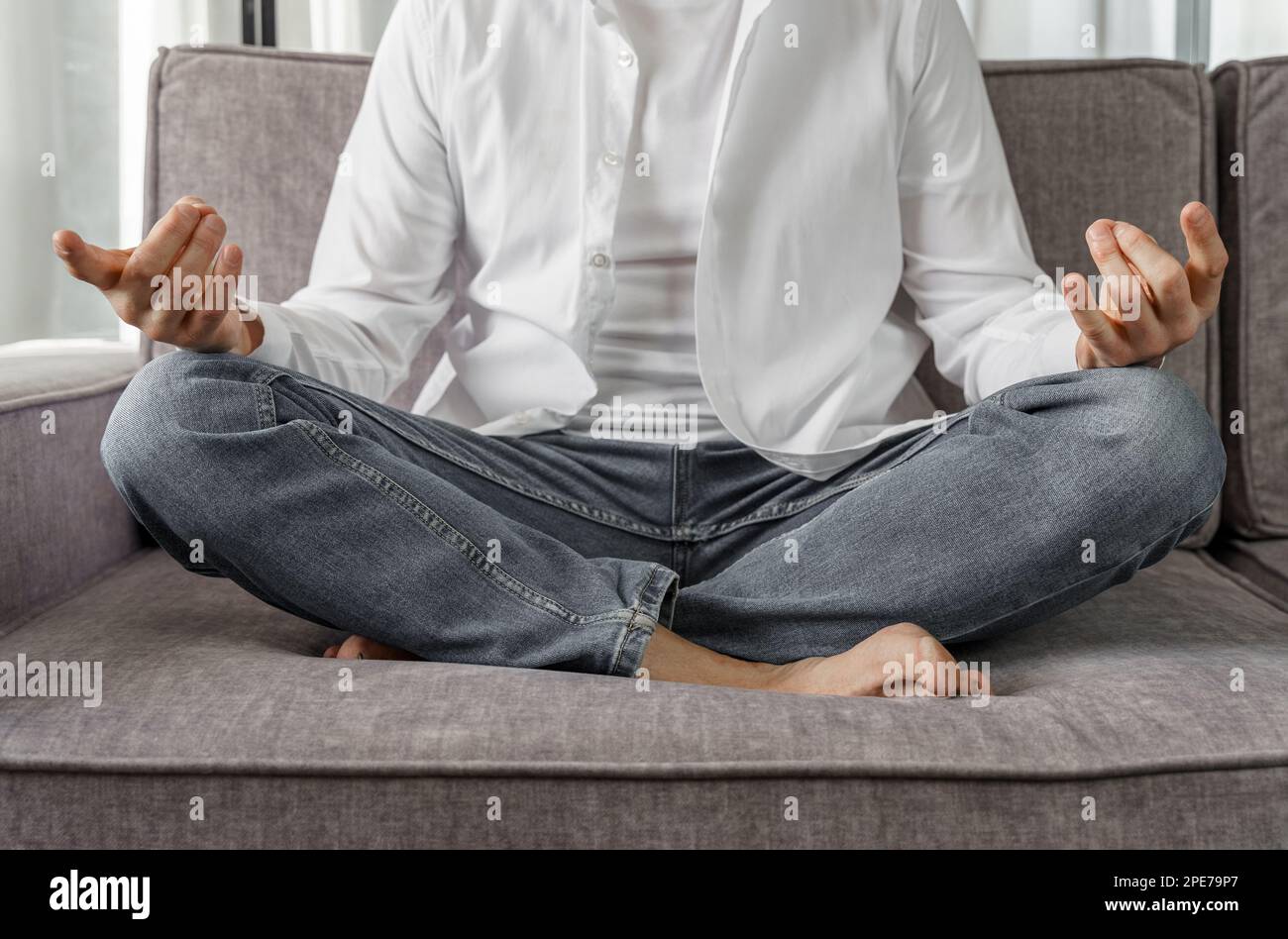Close-up of a man sitting on a sofa in the lotus position. Close-up ...