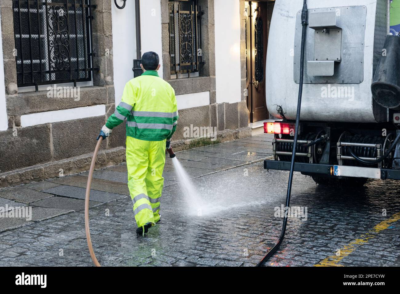 Worker cleaning with pressure water a street of a historic town. City ...