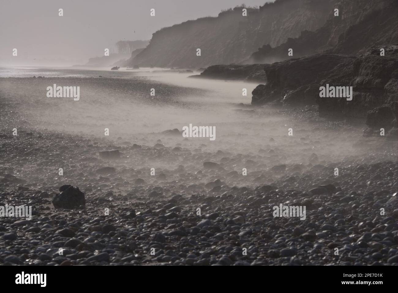 Windswept sand on beach, with pebbles partly covered in sand, crumbling ...