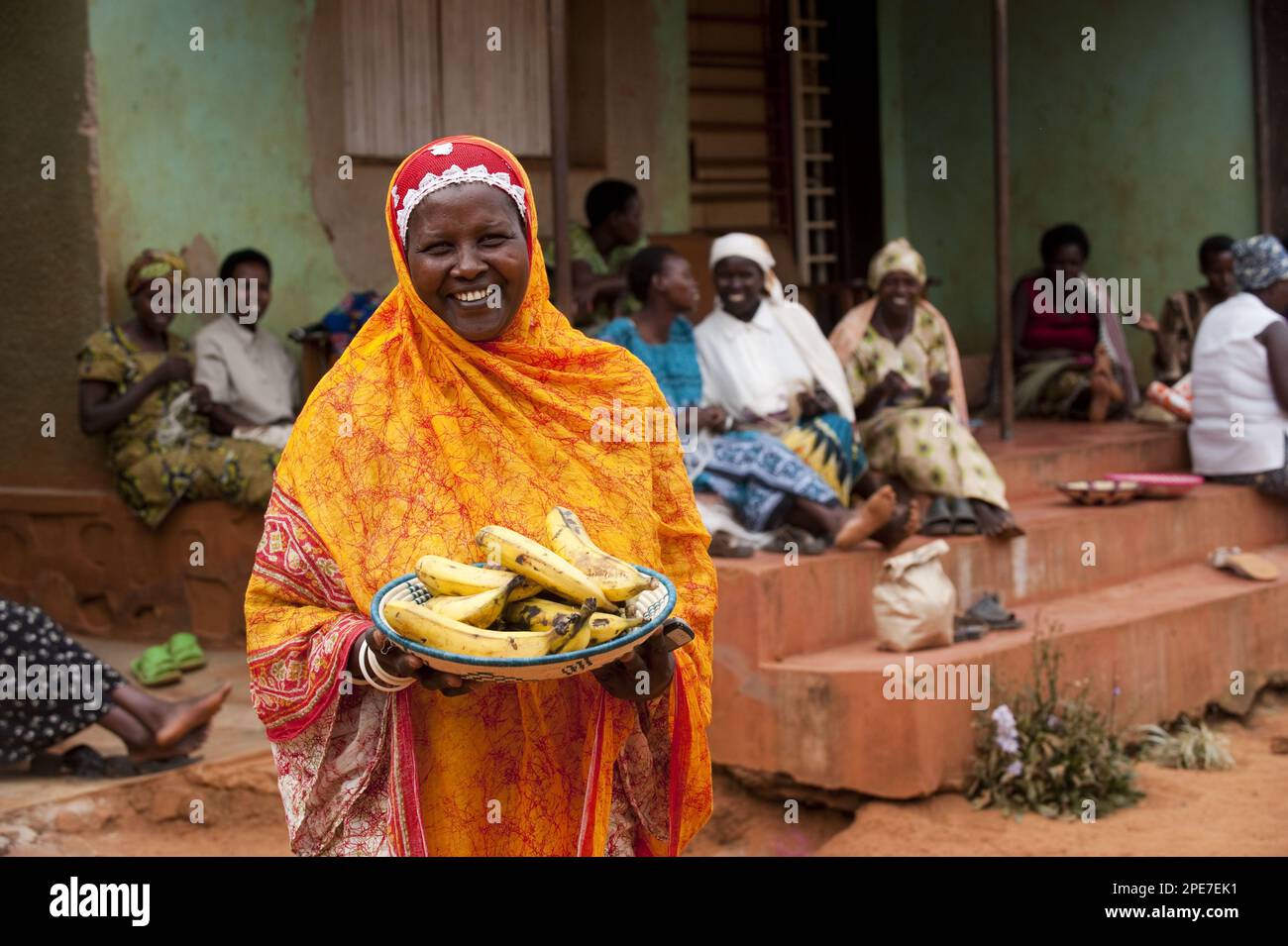 Smiling Muslim lady with light headscarf, holding a basket of bananas ...