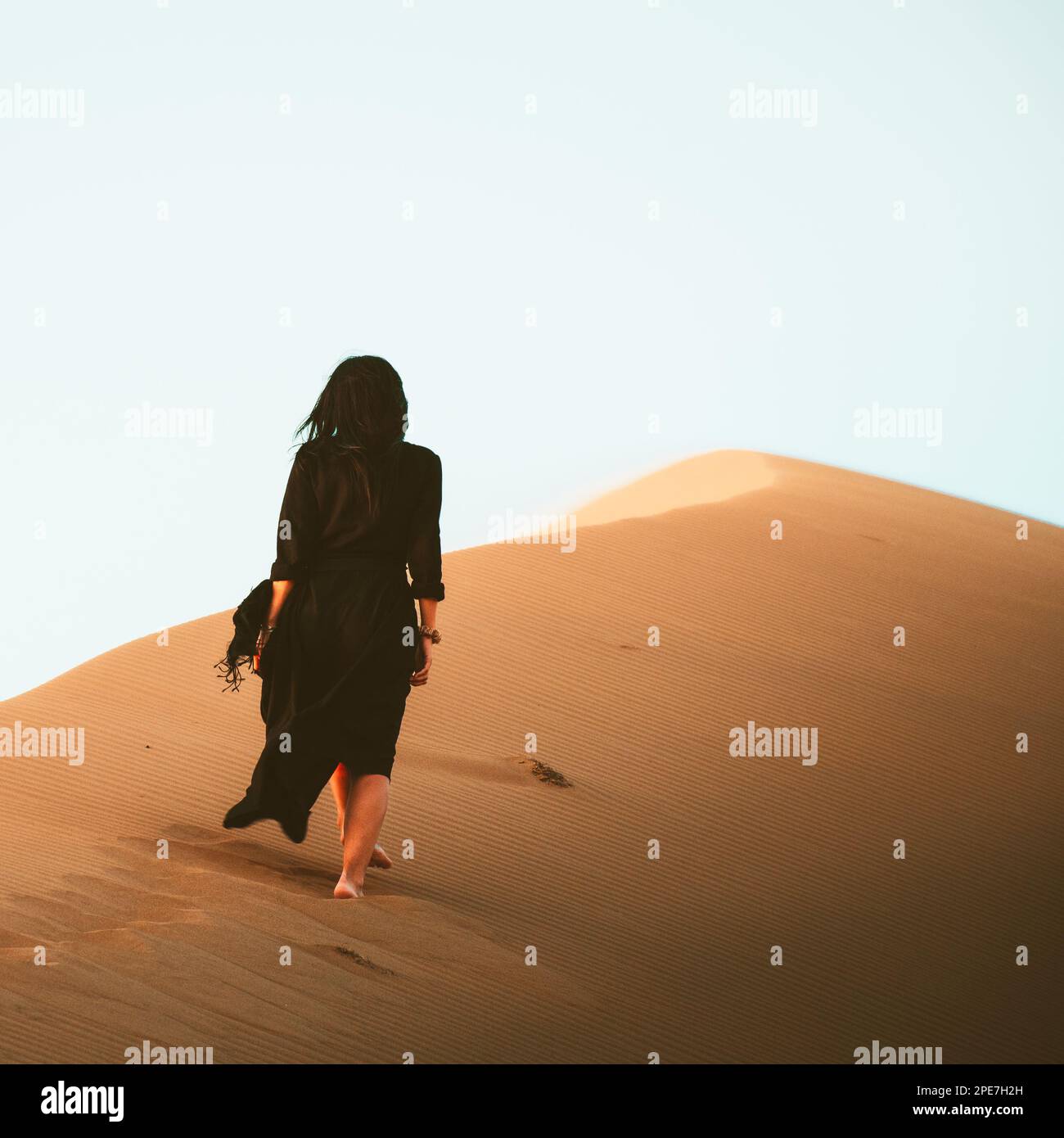 Young beautiful woman in long dress walks along sand dunes reaching top ...