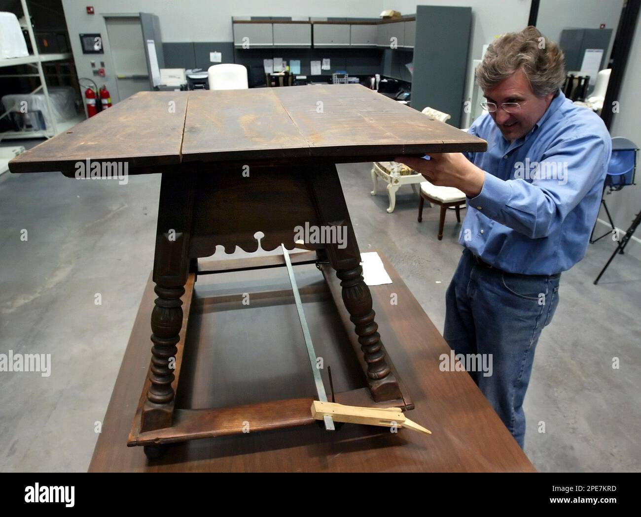 Furniture conservator David deMuzio places the desktop onto the lower portion of a desk which ...