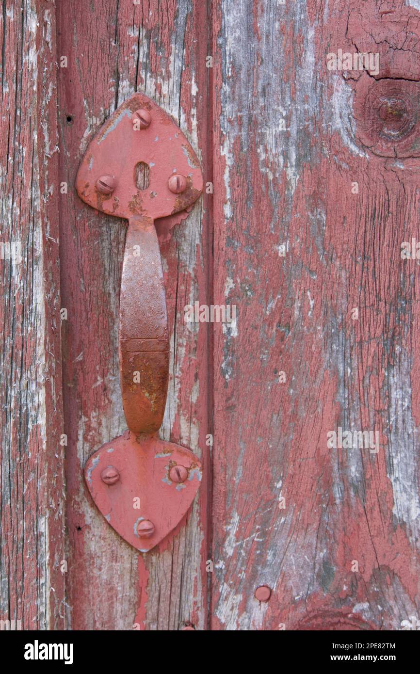 Close up of painted red, metal handle on old barn with peeling paint ...