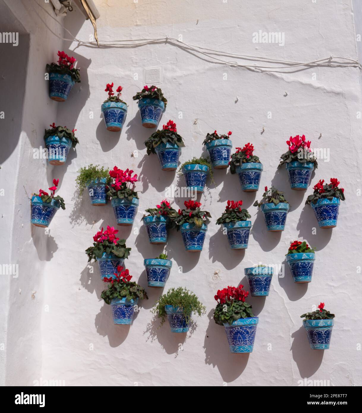 Colourful Spanish flower pots blue with red flowers on white wall in ...