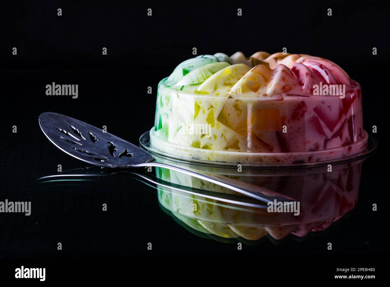 A rainbow coloured jelly mold dessert reflecting on a glass table ...