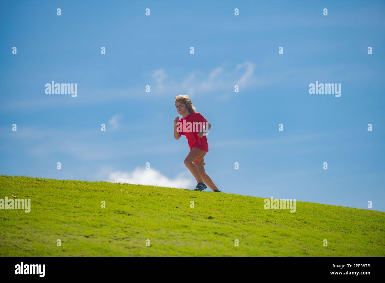 Cute boy running across grass and summer sky. Sporty child boy runner ...