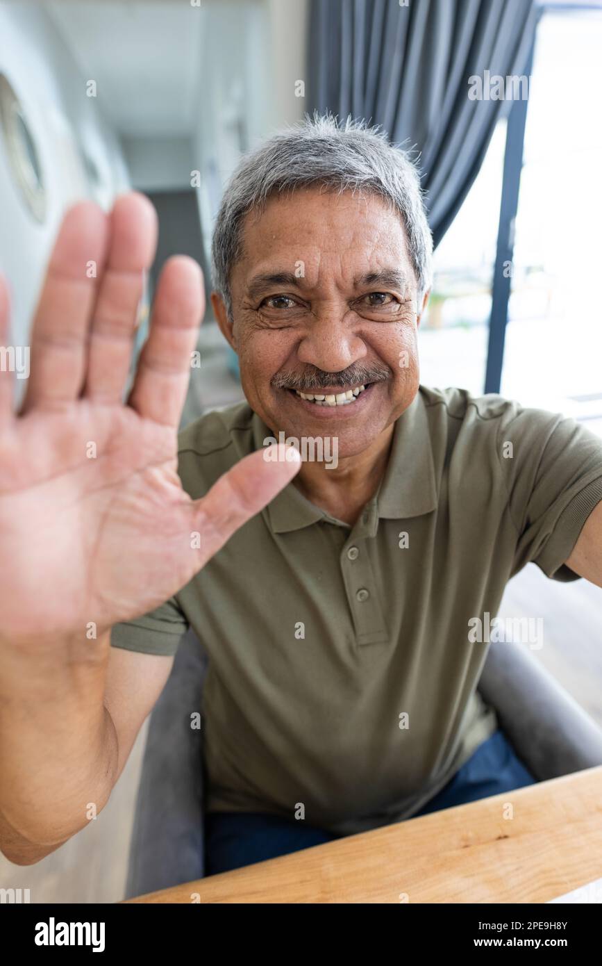 Close-up portrait of cheerful biracial senior man waving hand while ...