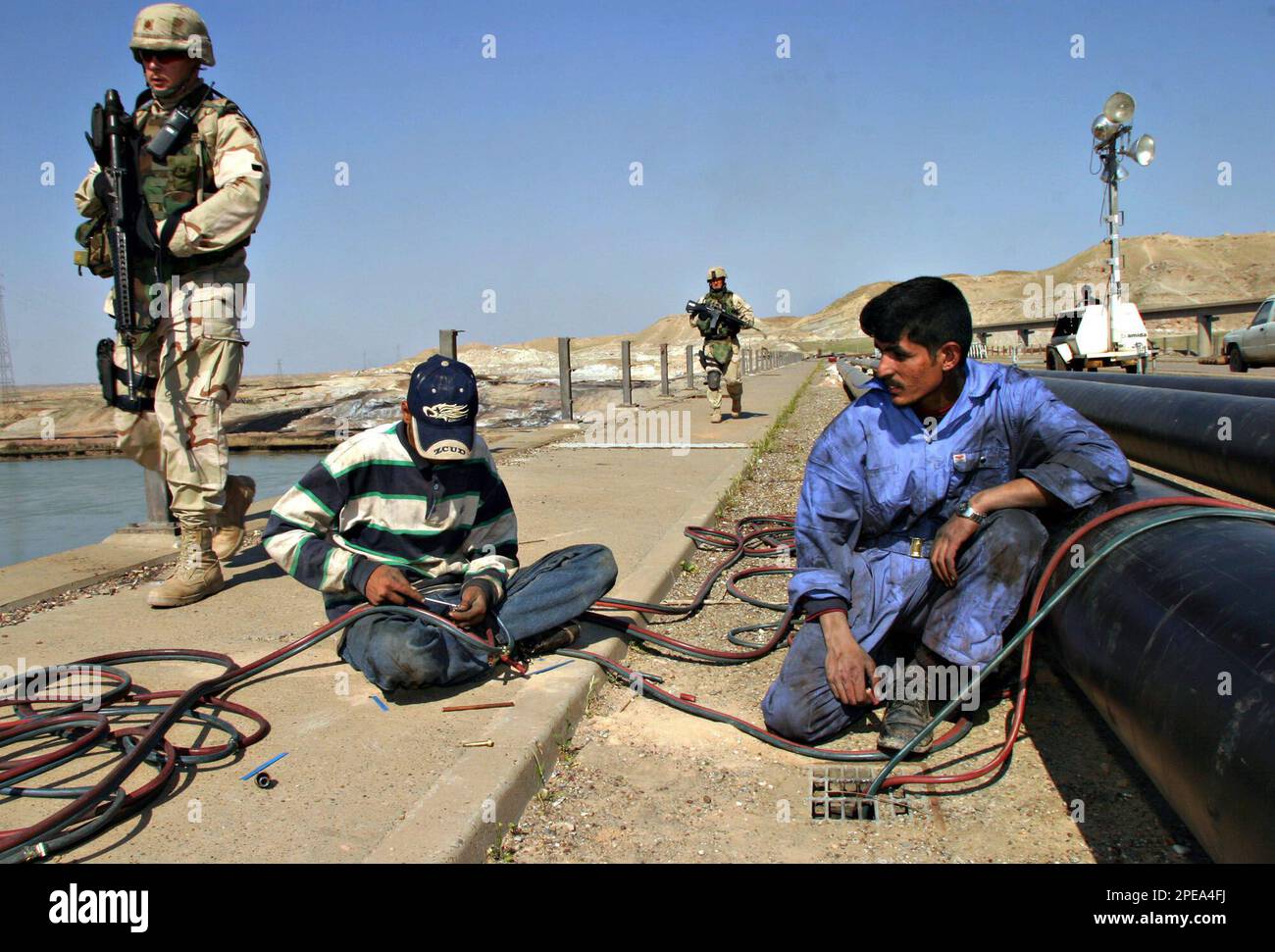 Iraqi workers maintain an oil pipeline as U.S. Army 42nd Infantry ...