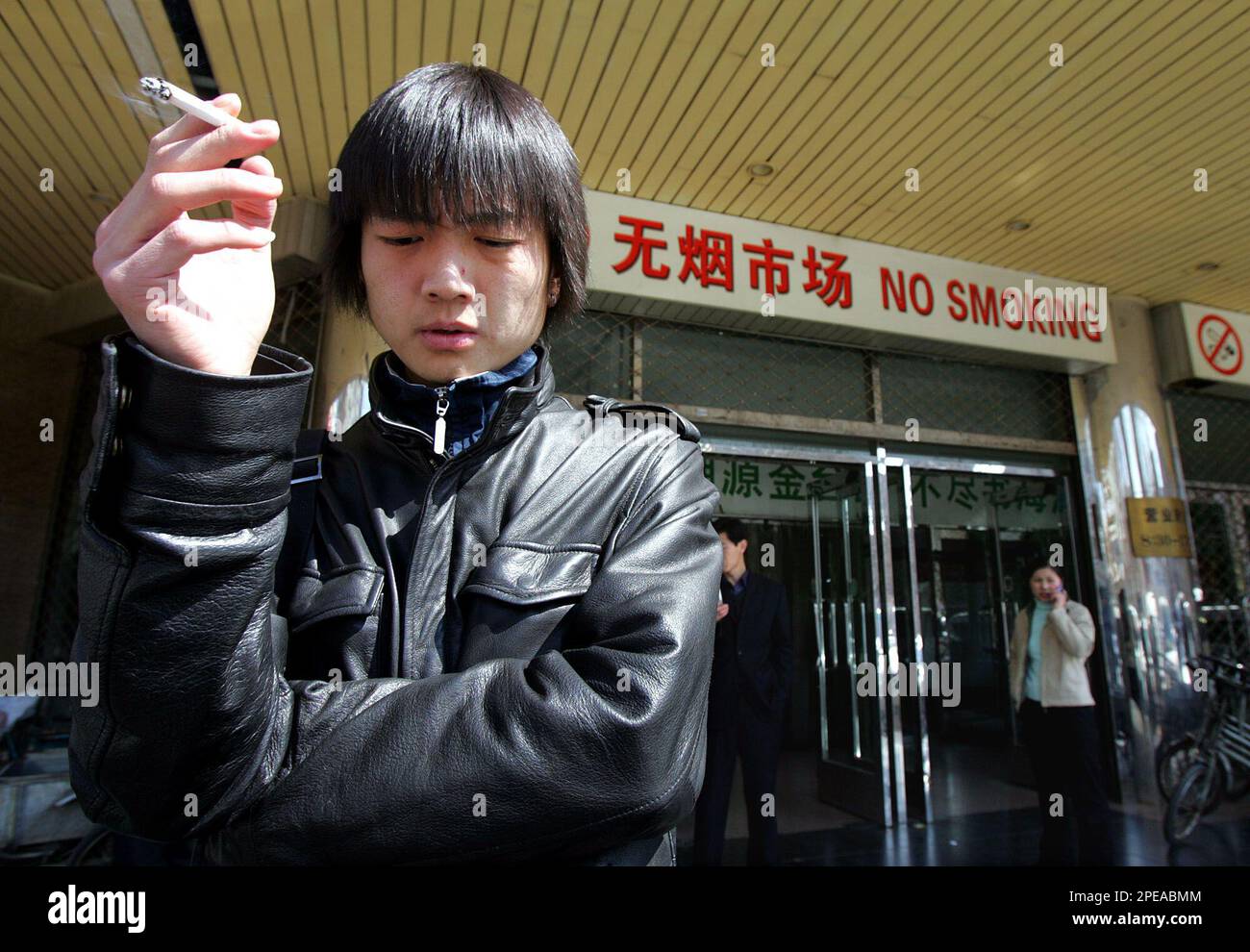 A youth smokes outside a store where a large no smoking sign has been ...