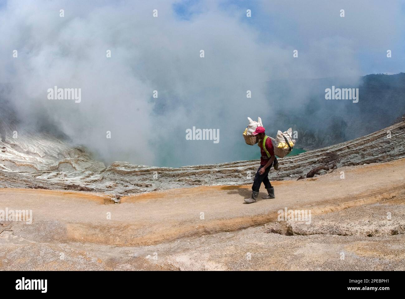 Local man carrying blocks of sulphur in baskets walking by crater with ...
