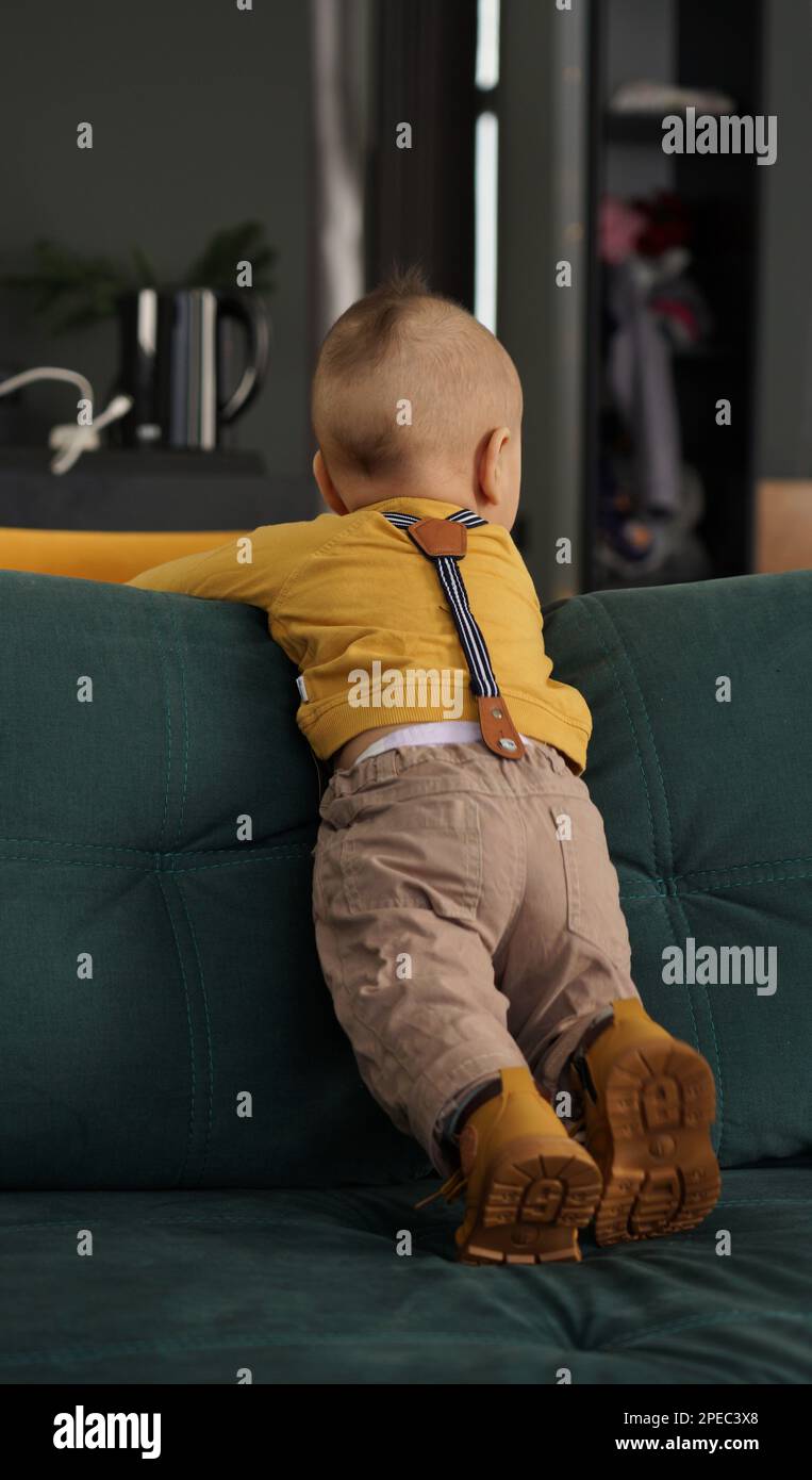 Back view of an infant kid in yellow clothes standing on green sofa ...
