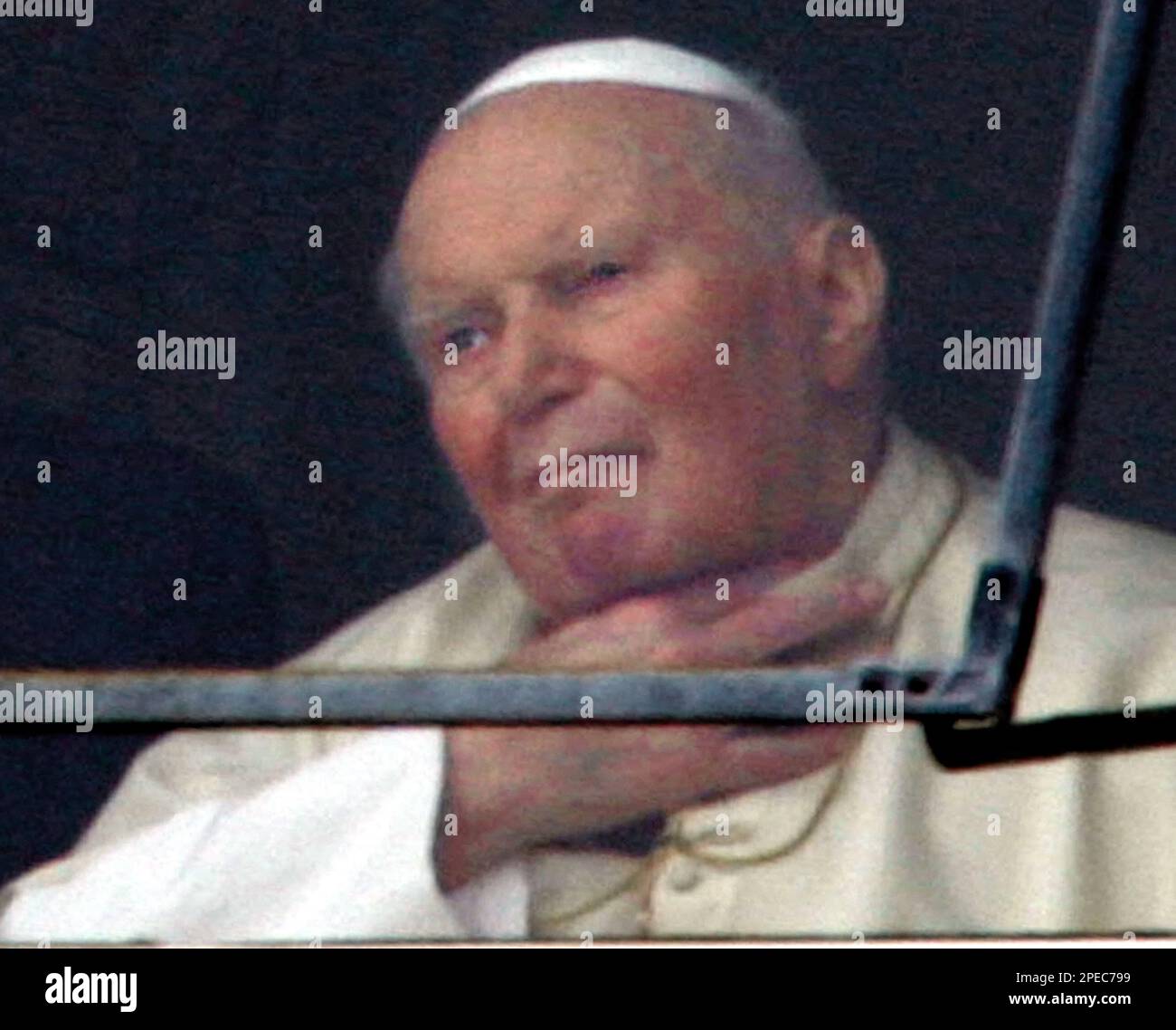 Pope John Paul II touches his neck, as he looks out from behind a ...