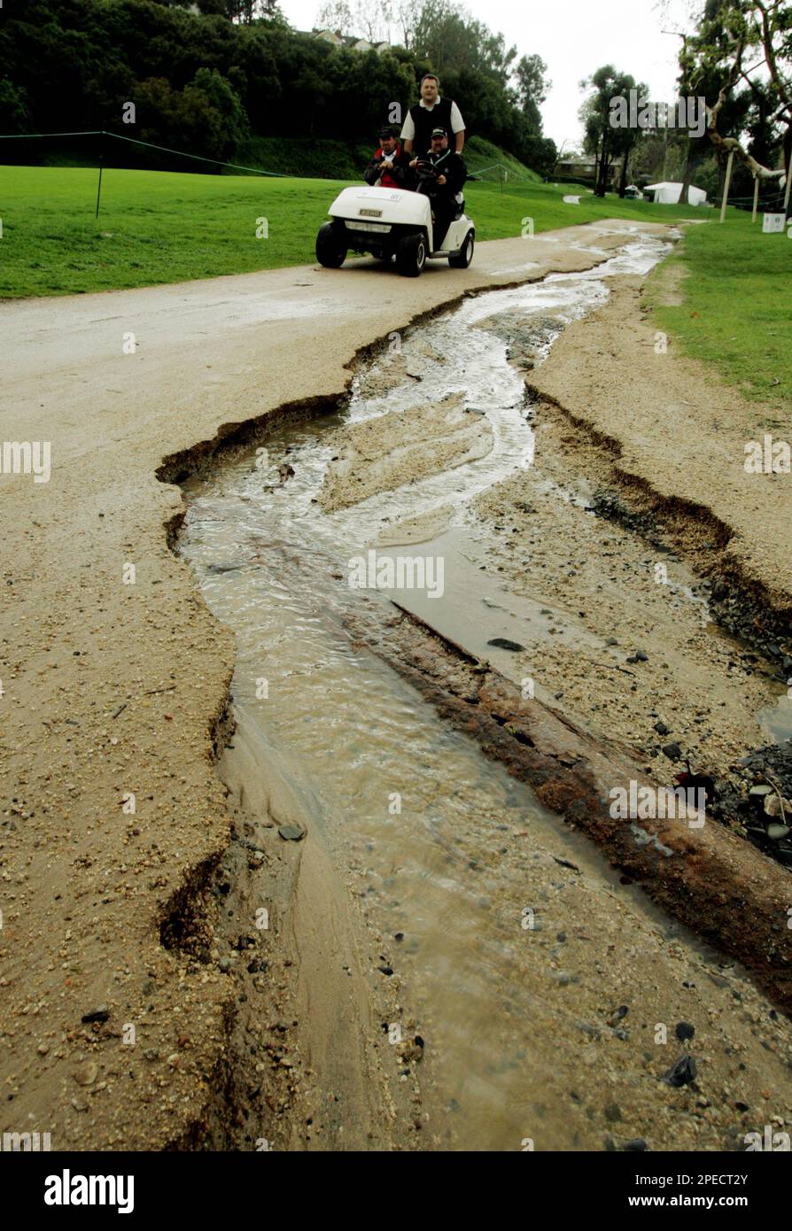 Course workers ride past a washed-out section of a cart path at Riviera ...