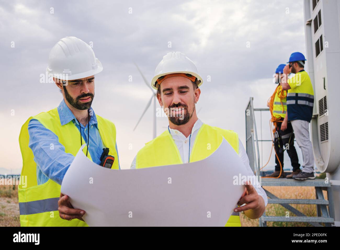 Two windmill engineers looking a blueprint with the plan of the ...