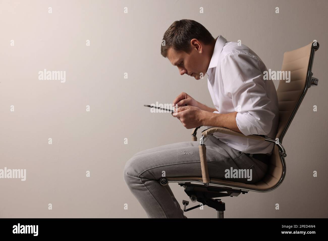 Man with bad posture using tablet while sitting on chair against grey ...