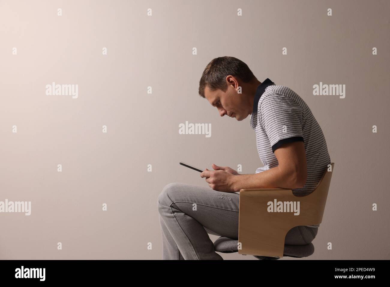 Man with bad posture using tablet while sitting on chair against grey ...