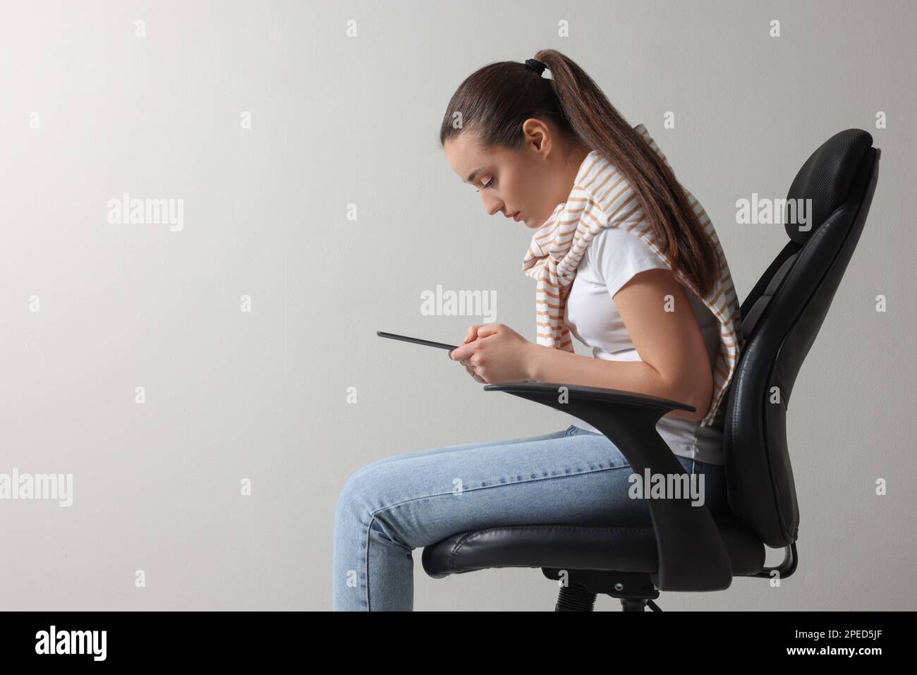 Young woman with poor posture using tablet while sitting on chair ...