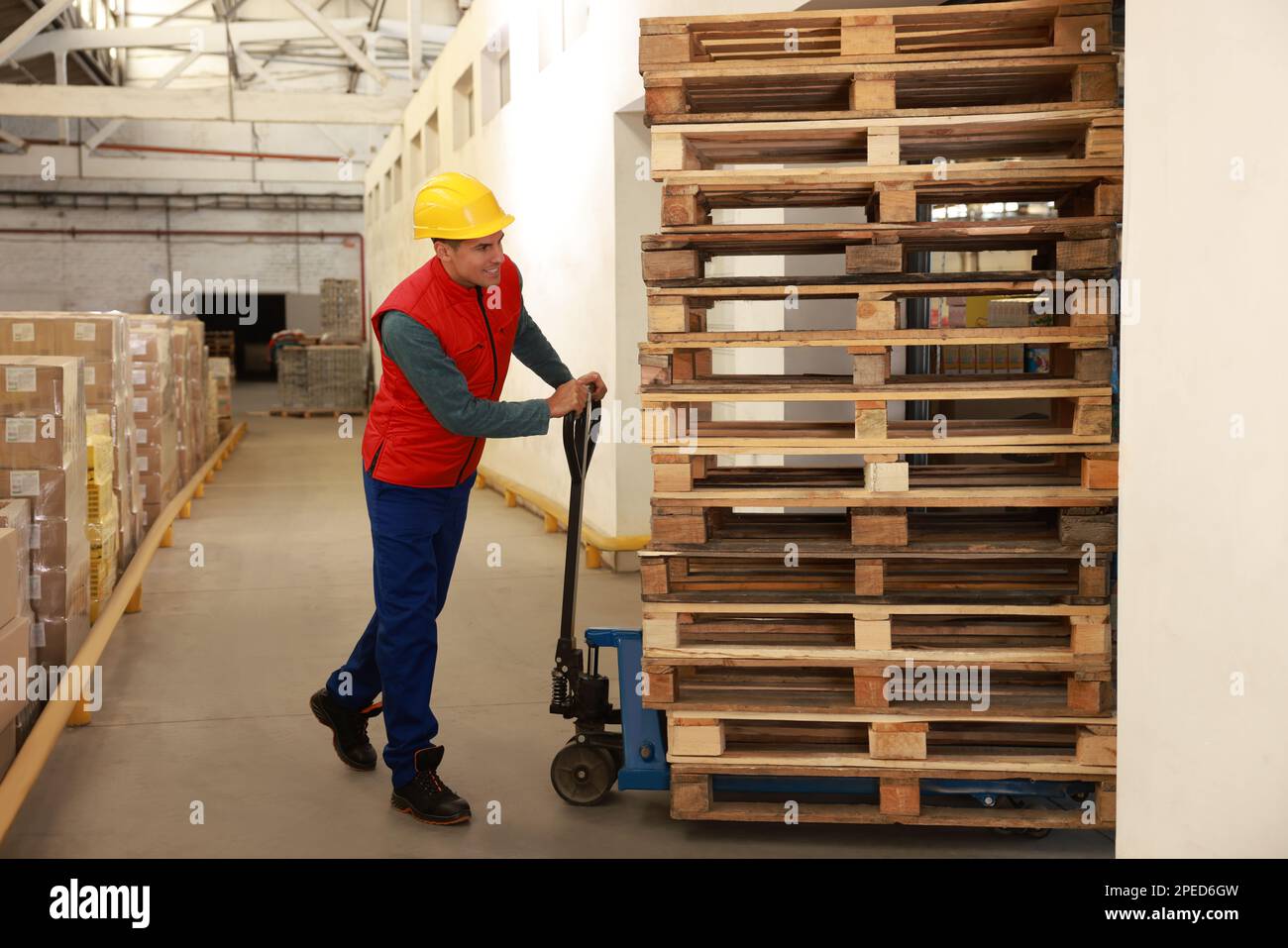 Worker moving wooden pallets with manual forklift in warehouse Stock ...