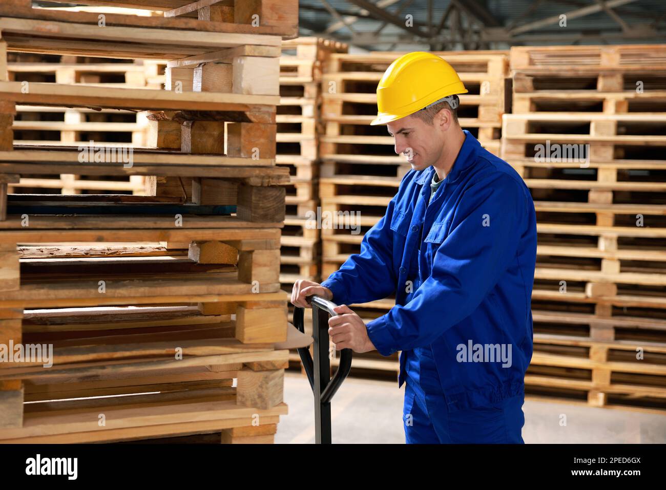 Worker moving wooden pallets with manual forklift in warehouse Stock ...