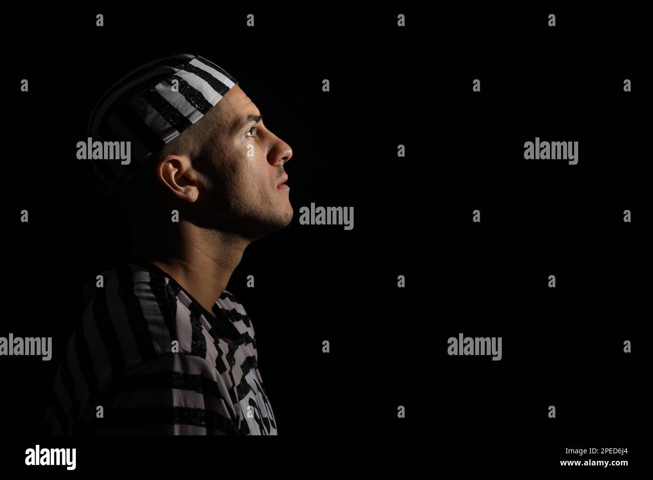 Remorseful prisoner in striped uniform on black background, space for ...