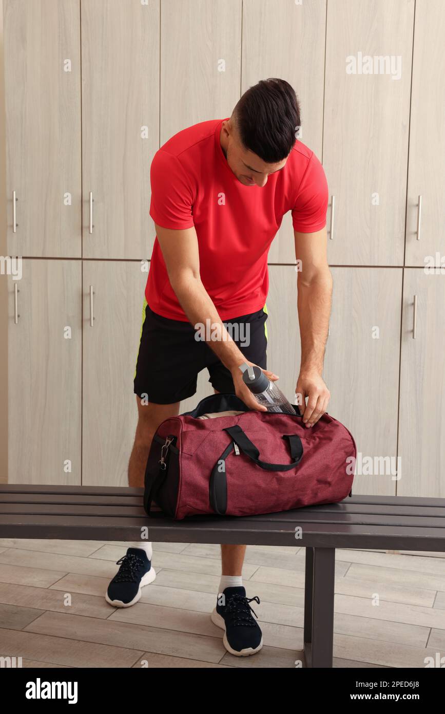 Handsome man putting bottle into sports bag in locker room Stock Photo ...