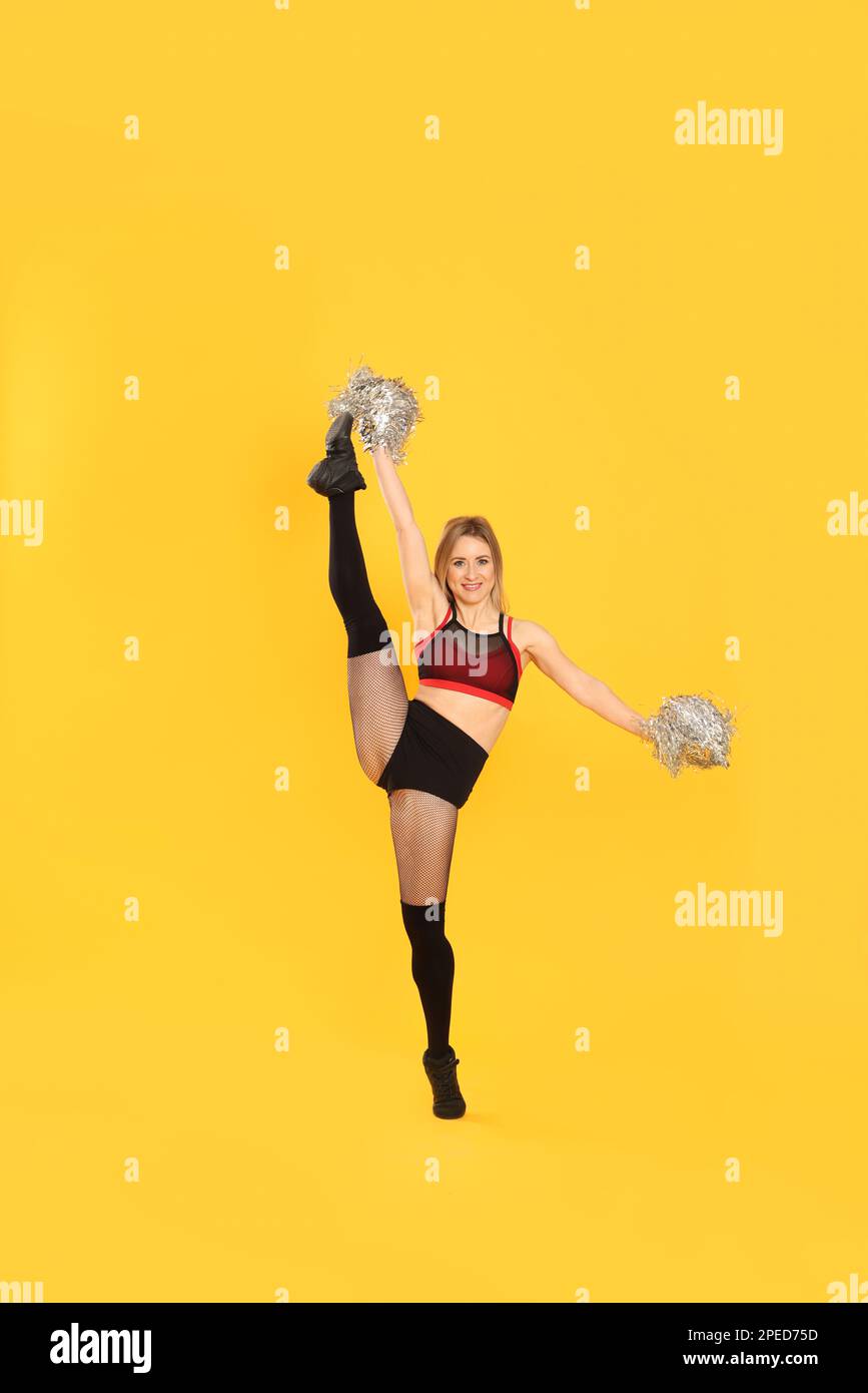 Beautiful cheerleader in costume holding pom poms on yellow background ...