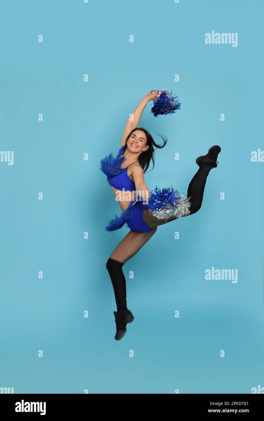 Beautiful cheerleader in costume holding pom poms on light blue ...