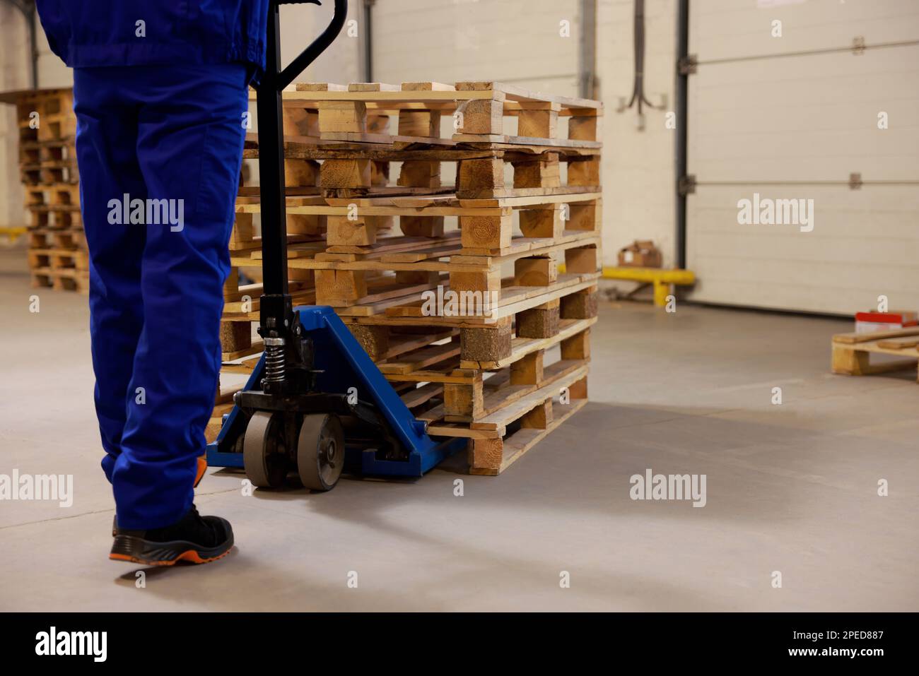Worker moving wooden pallets with manual forklift in warehouse, closeup ...