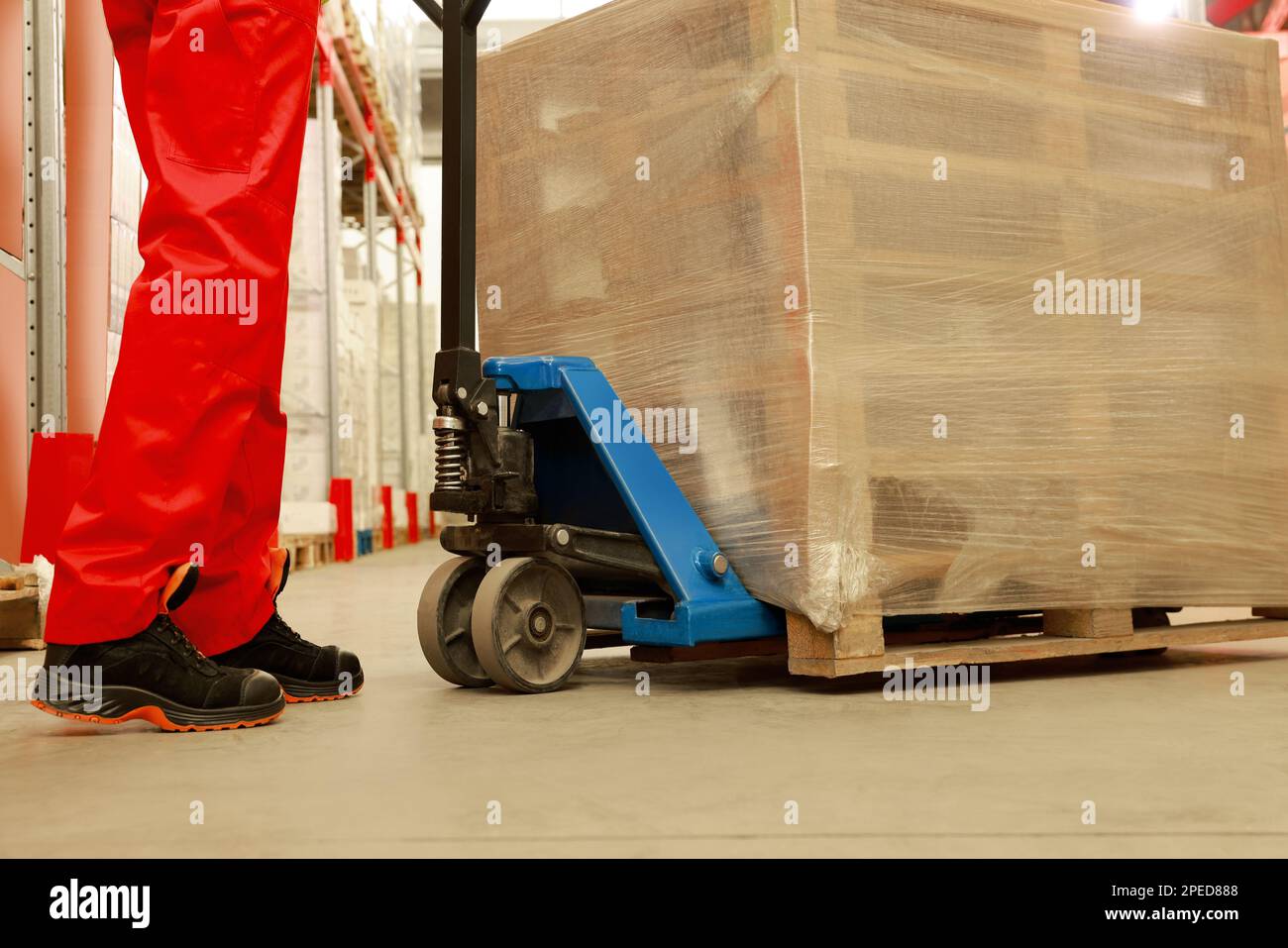 Worker moving wrapped wooden pallets with manual forklift in warehouse ...