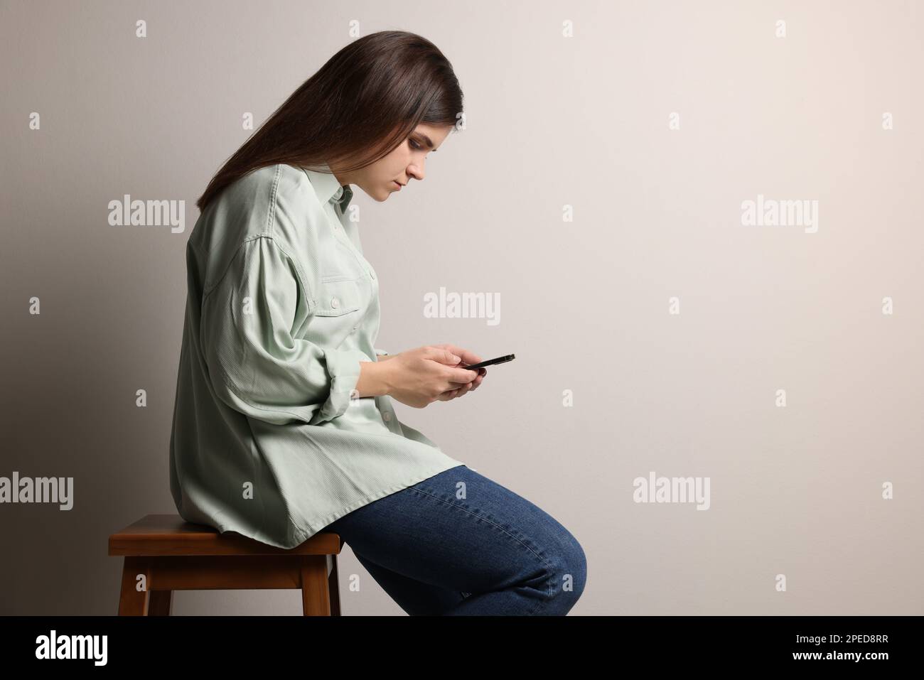 Young woman with bad posture using smartphone while sitting on stool ...