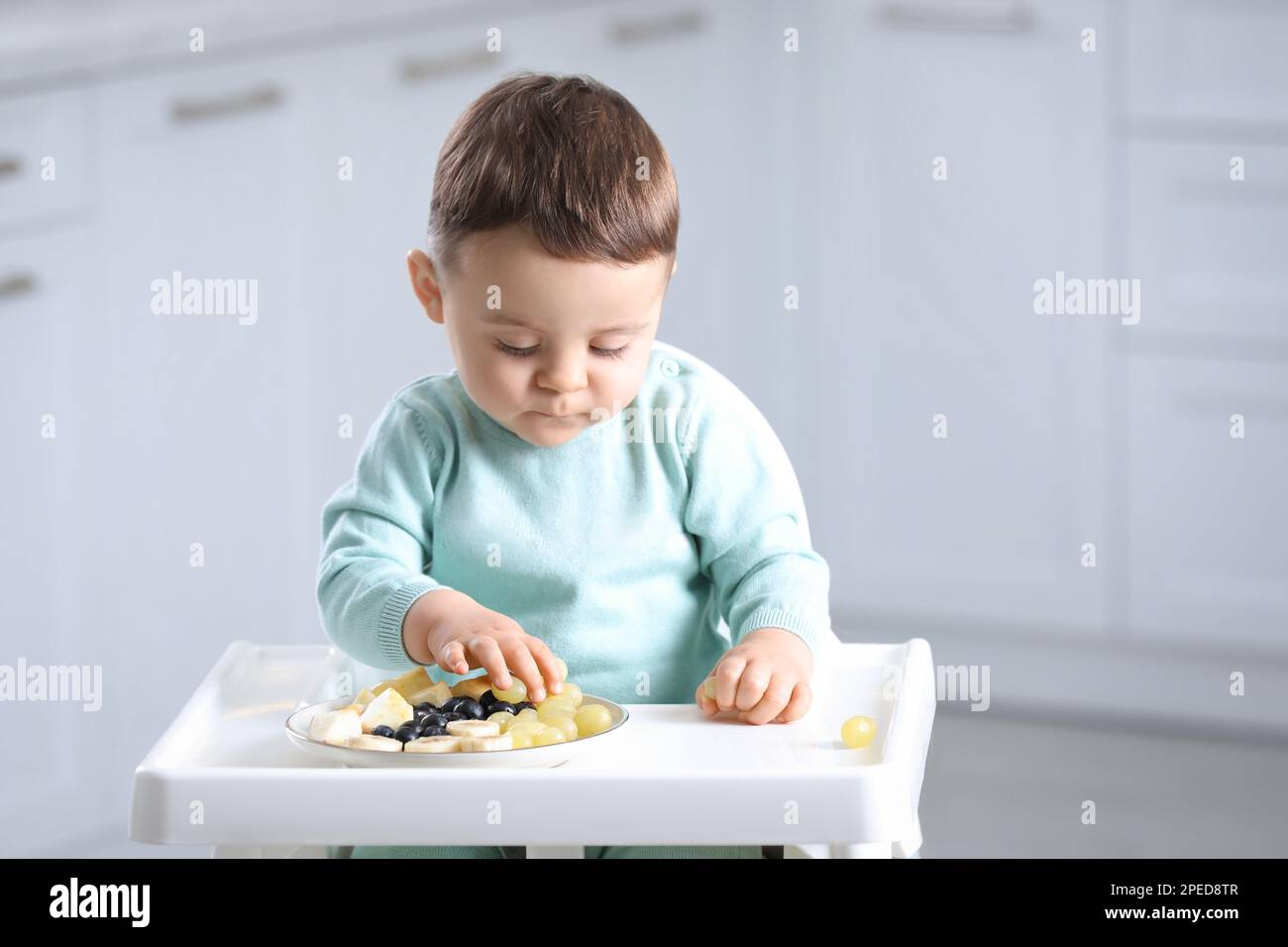 Cute little baby eating healthy food in high chair at home. Space for ...