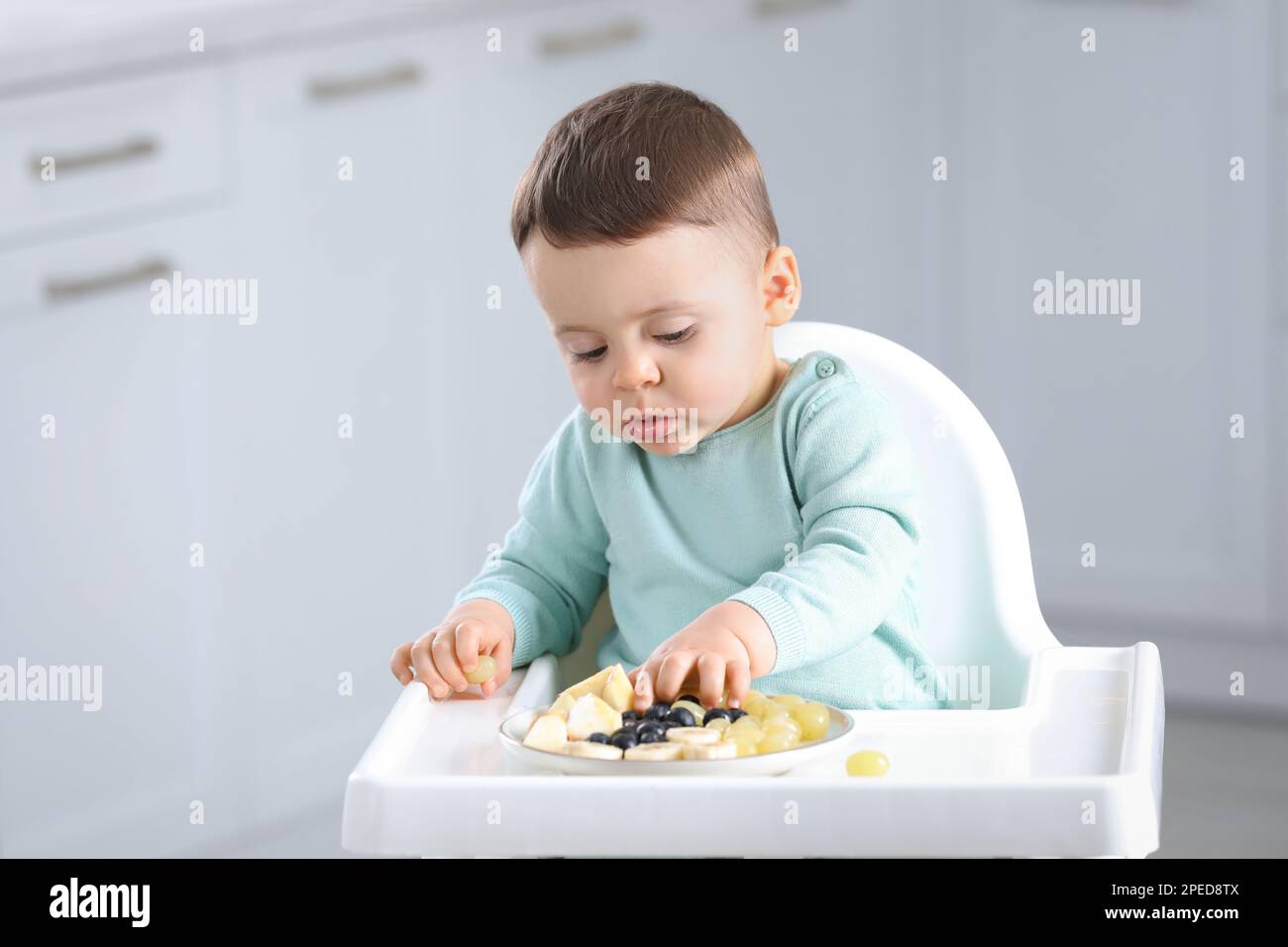 Cute little baby eating healthy food in high chair at home Stock Photo ...