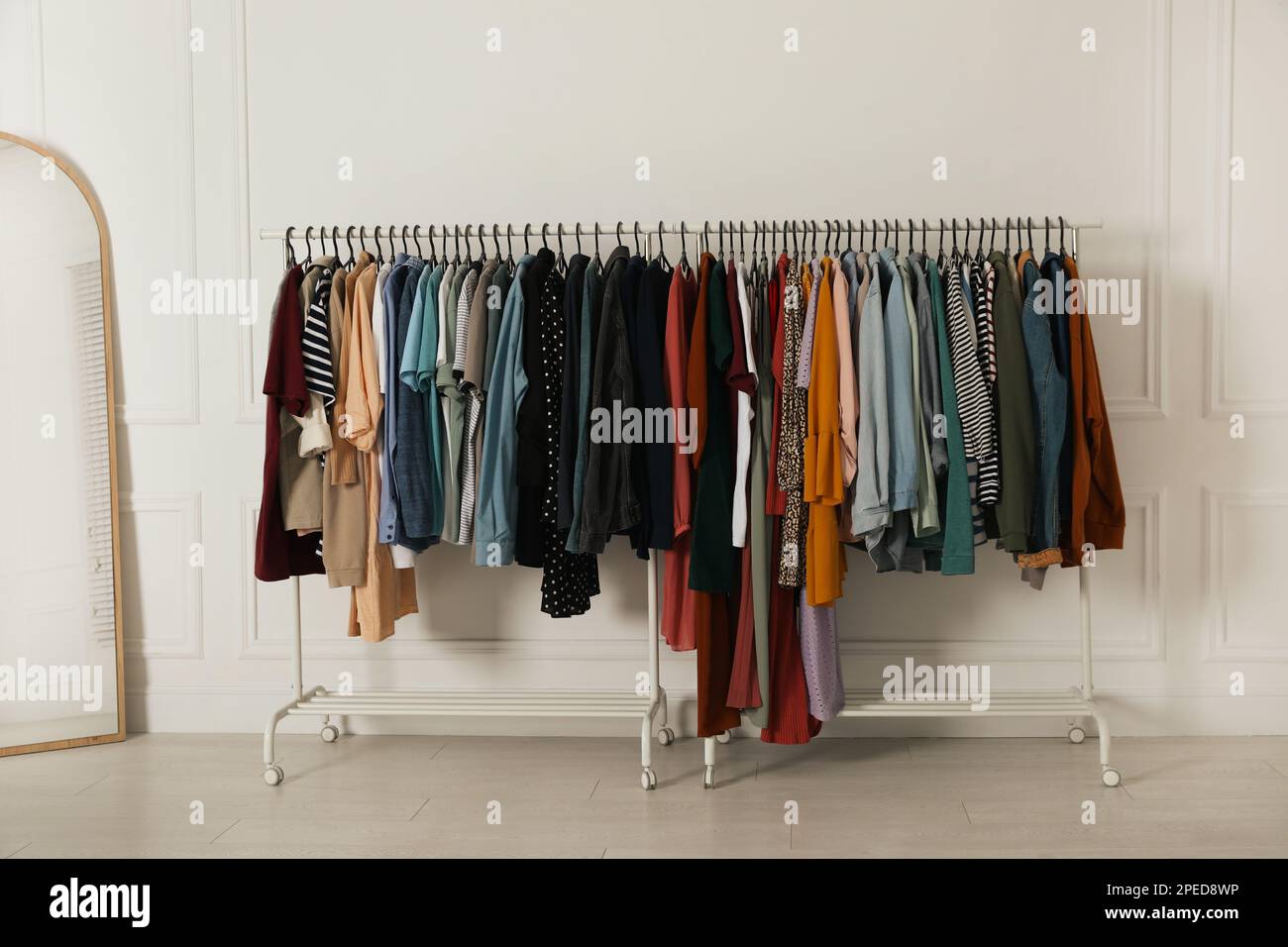Racks with stylish clothes and mirror near white wall indoors. Fast ...