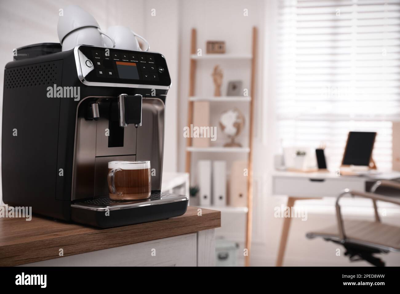 Modern espresso machine with glass cup of coffee on table in office ...