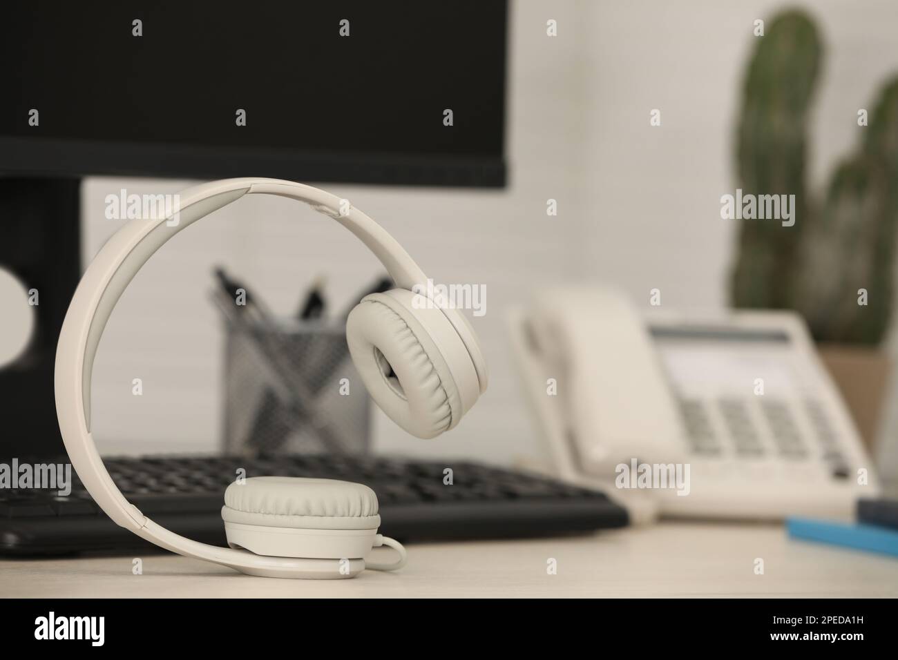 Modern headphones, desktop telephone and computer on table indoors ...