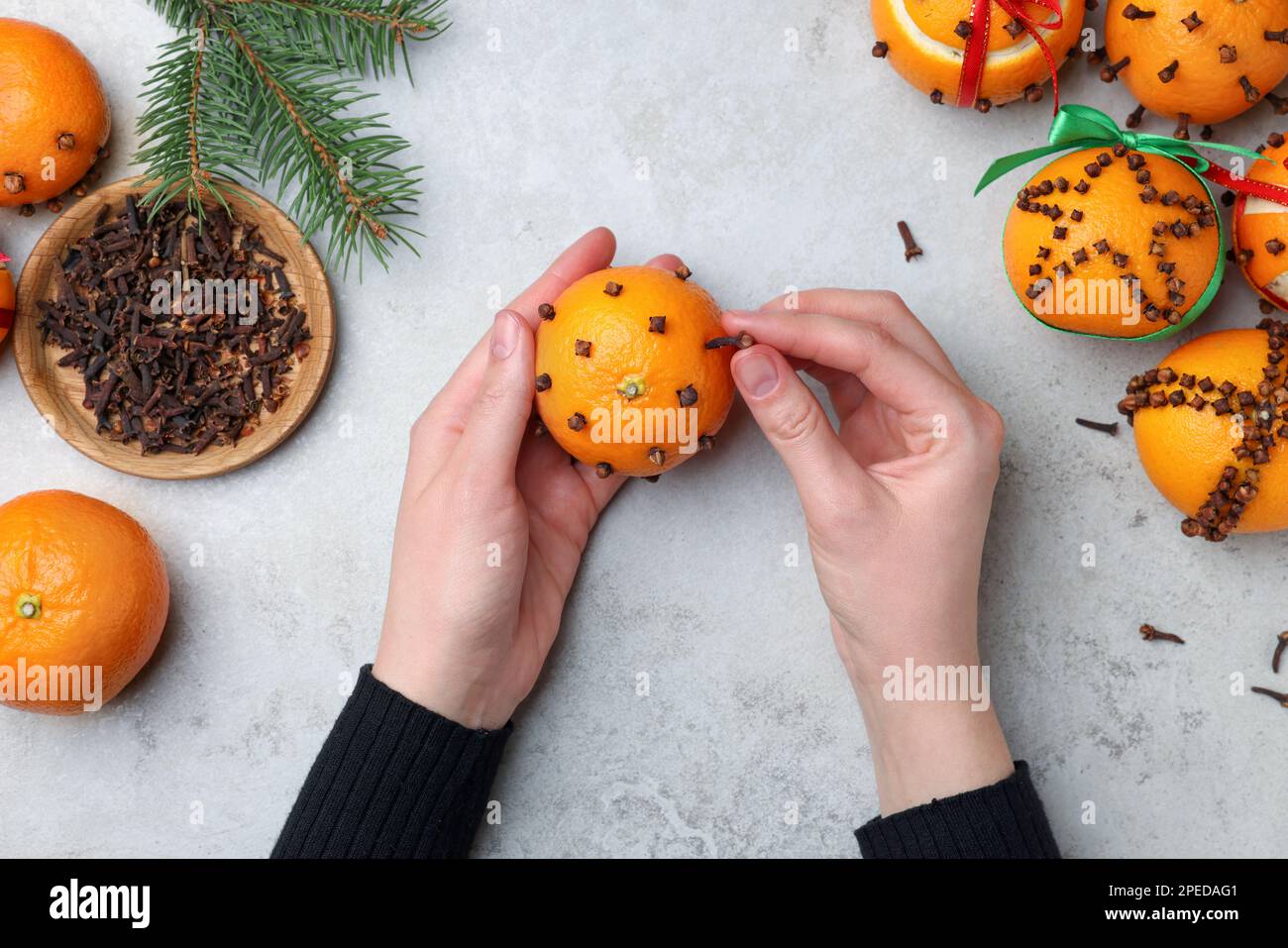 Woman decorating fresh tangerine with cloves at grey table, top view ...
