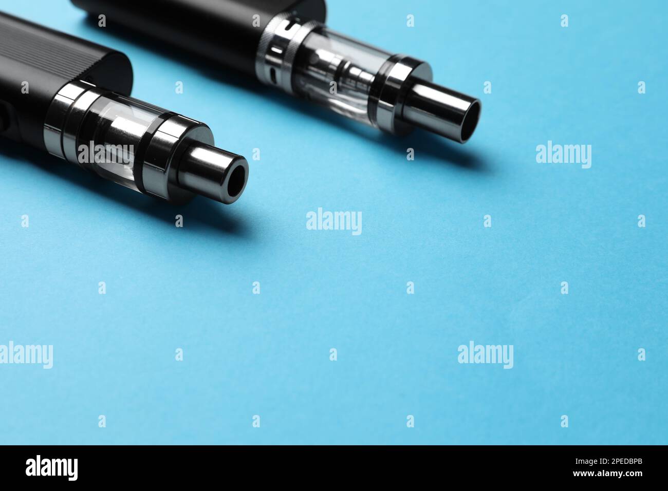 Two electronic cigarettes on light blue background, closeup. Space for ...