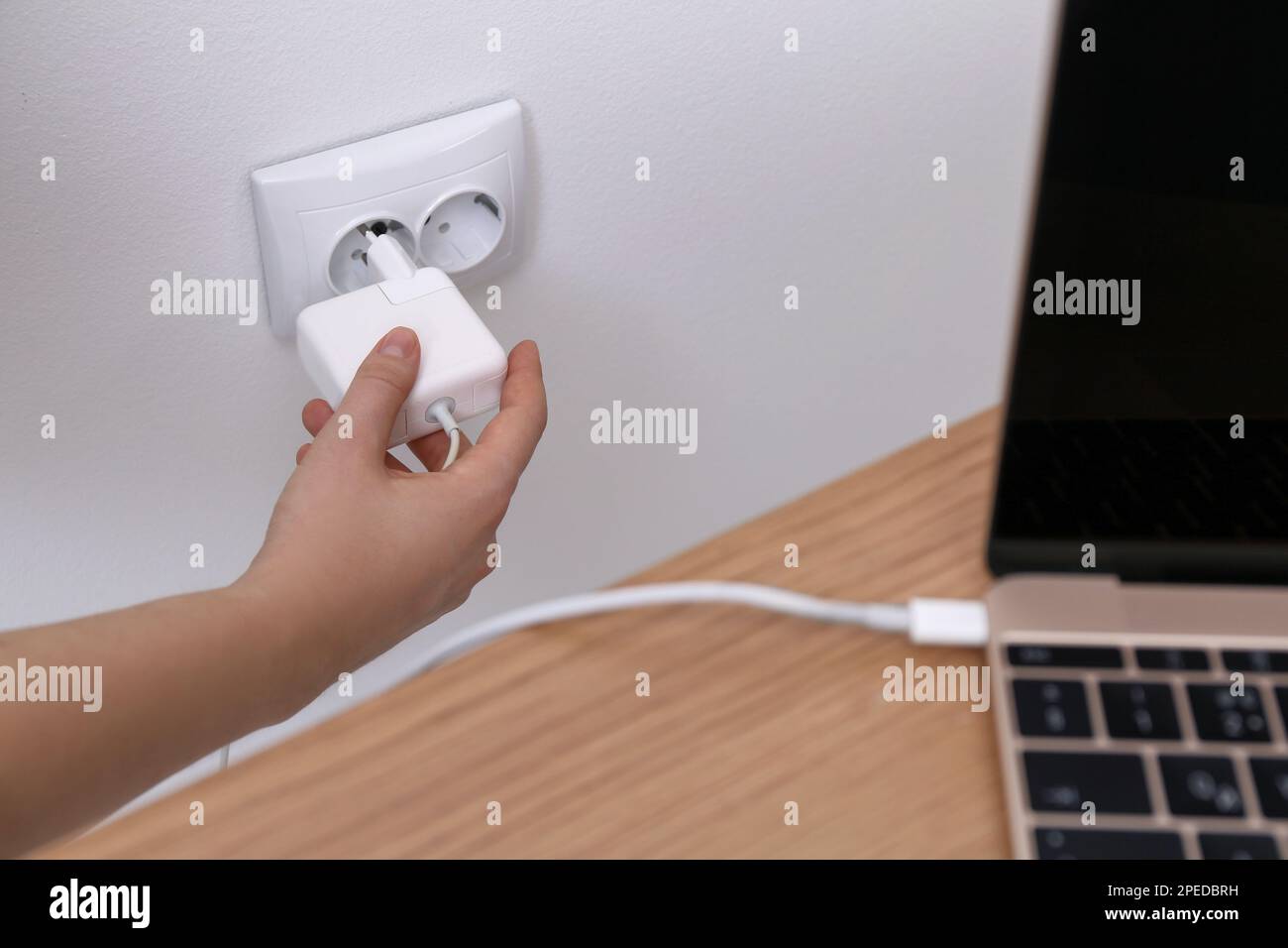 Woman inserting power plug for laptop charging into wall socket indoors ...