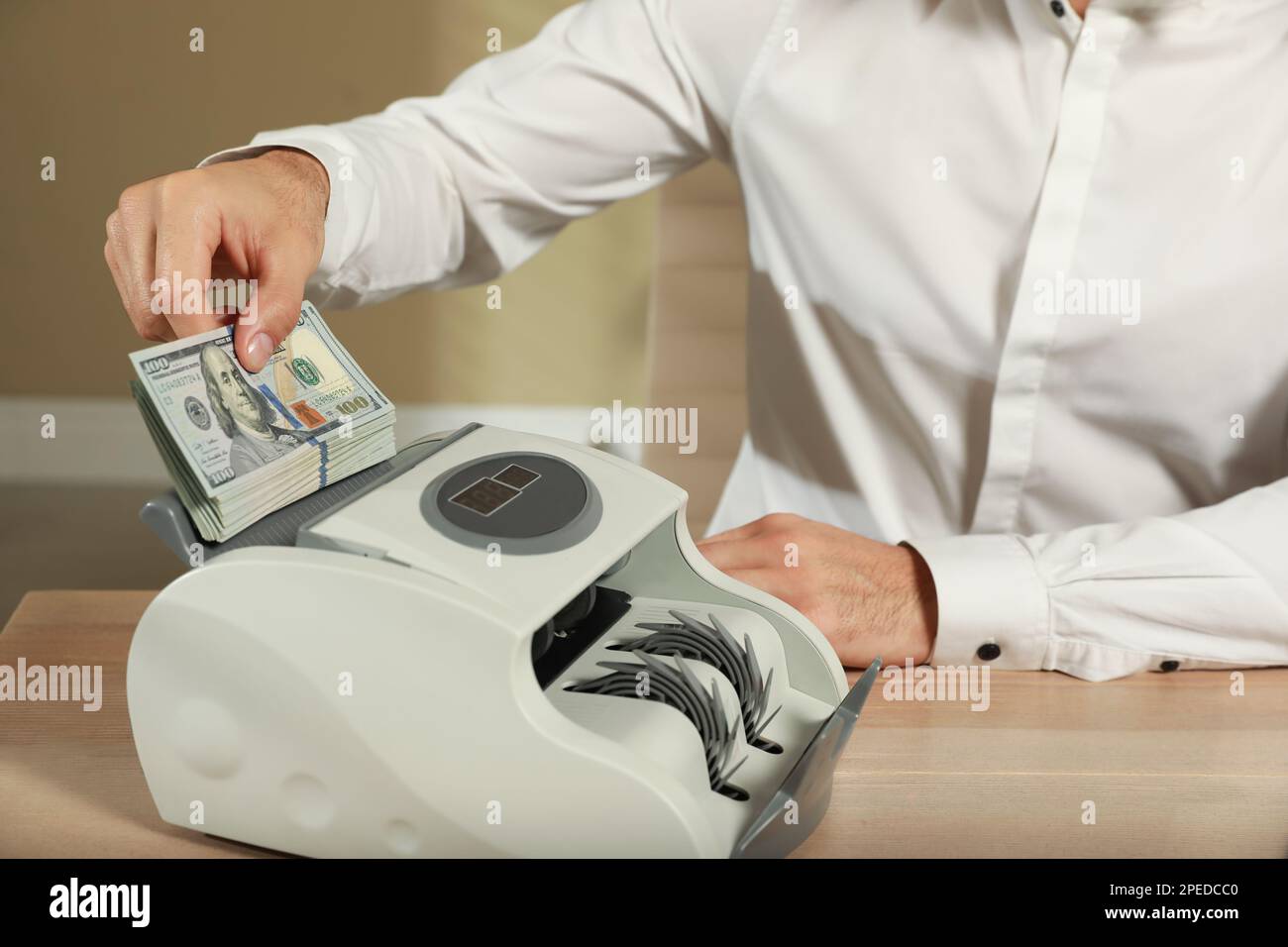 Man putting money into banknote counter at wooden table indoors ...