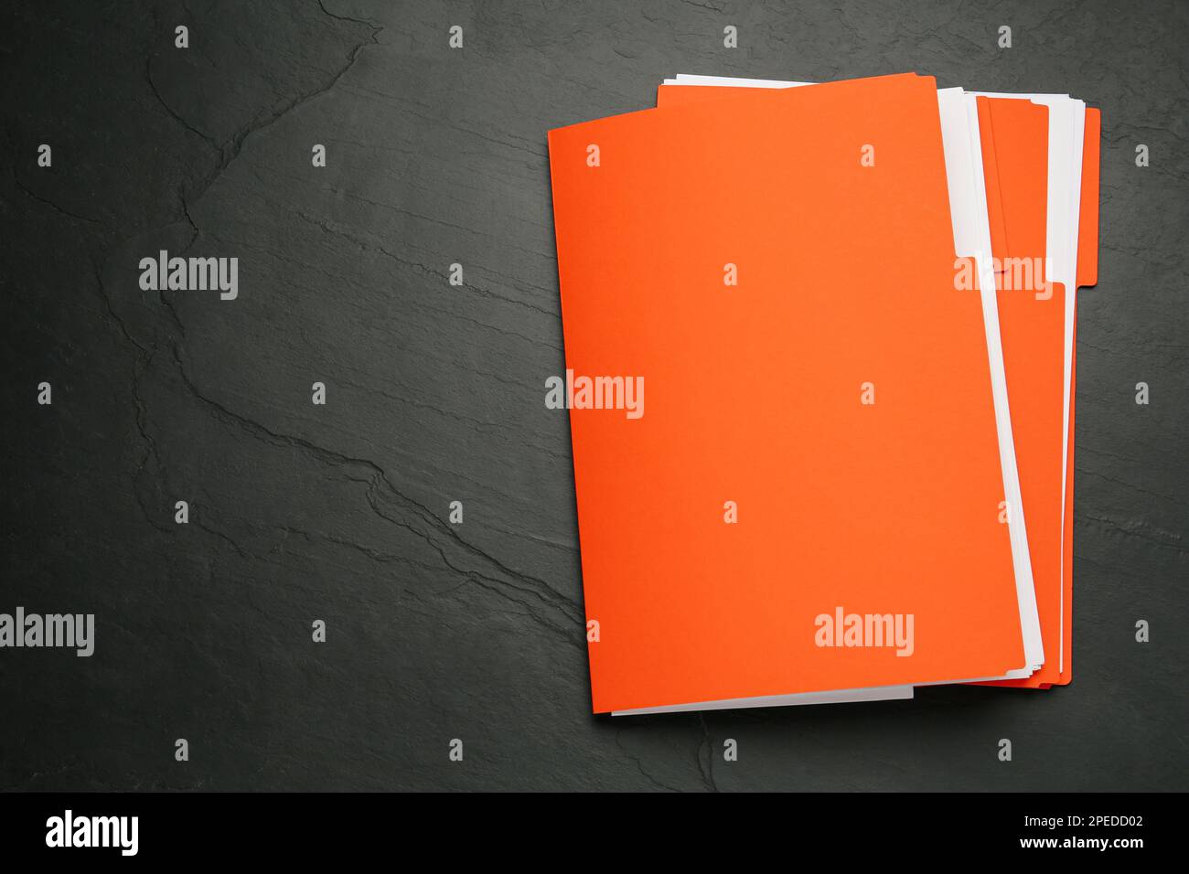 Orange files with documents on black slate table, top view. Space for ...